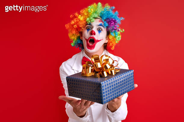 playful positive funny clown holding gift box in hands posing ...