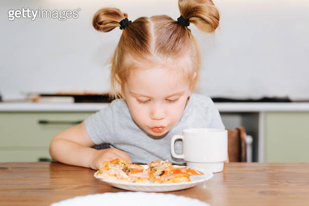 Little caucasian girl blowing on hot food while sitting at the table in ...