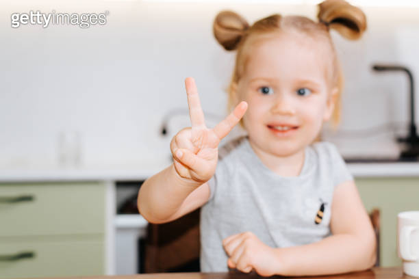 Cute smiling child girl showing peace sign gesture while sitting at ...