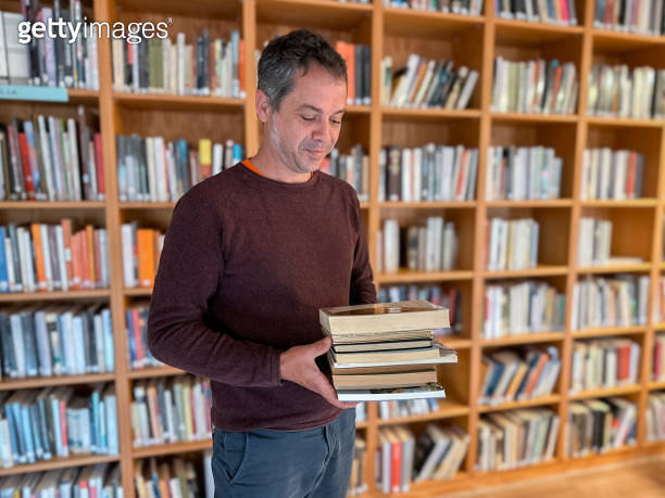 Librarian standing holding a stack of books in the library 이미지 ...