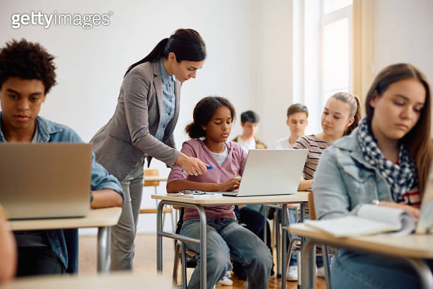 Computer science teacher assisting her student in using laptop during a ...