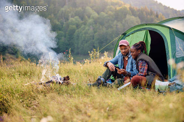 Happy couple using mobile phone while camping in nature. 이미지 ...
