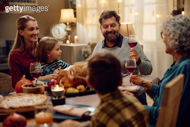 Happy father raising a toast during Thanksgiving dinner with his family ...