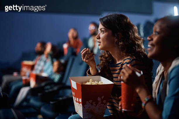 Young woman eating popcorn while watching suspenseful movie in cinema ...