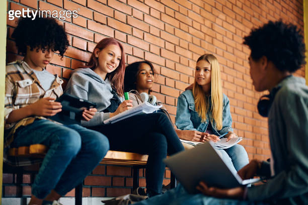 Multiracial group of high school friends talking while studying in a ...