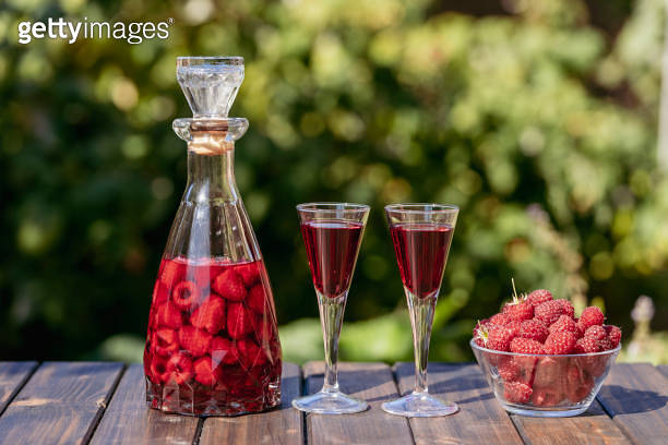 Homemade red raspberry brandy in two glasses and in a glass bottle on a ...