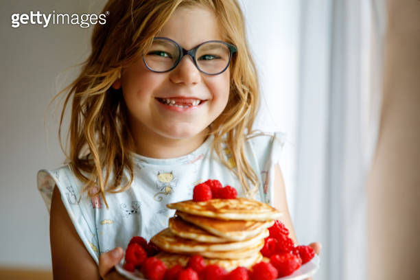 Little happy preschool girl with a large stack of pancakes and ...