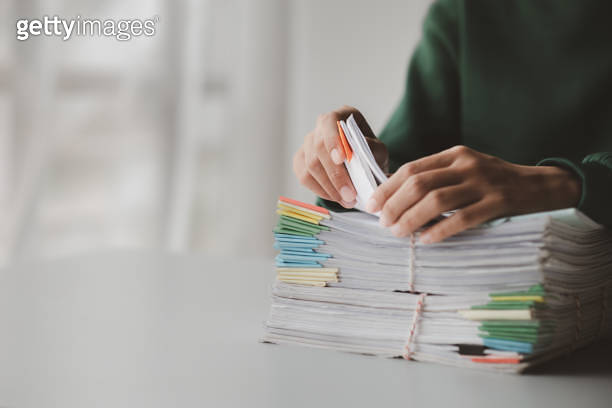 A person sits in an office with a huge stack of papers, she is a ...