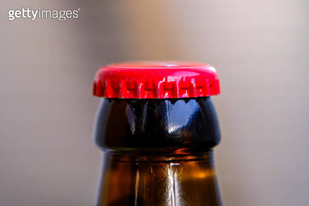Brown glass beer bottle neck with red metal cap. close-up of unopened ...