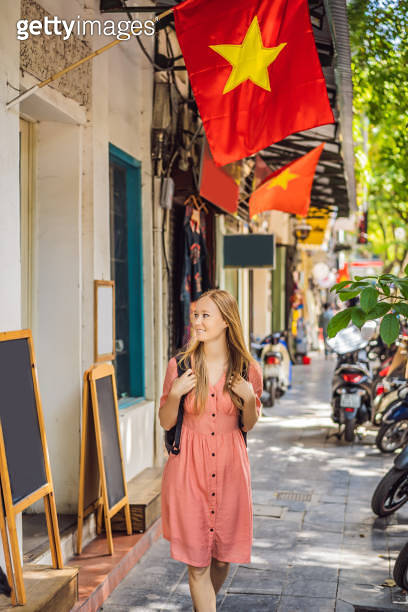 Woman tourist with backpack walks on vietnamese street with flags ...