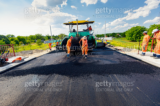 Asphalt spreader, tarmac road laying machine. Workers with shovels ...