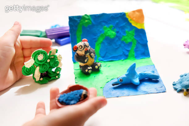 Child smearing colorful plasticine on cardboard and creating fairy tale ...