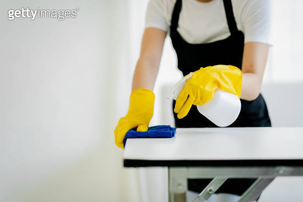 Young women use cleaning cloths and disinfectant sprays to wipe tables ...