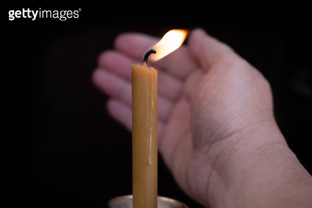 Close-up candle in dark, female hands shield burning flame from wind ...