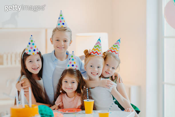 Group of adorable kids wear party hats, embrace and have fun, celebrate ...