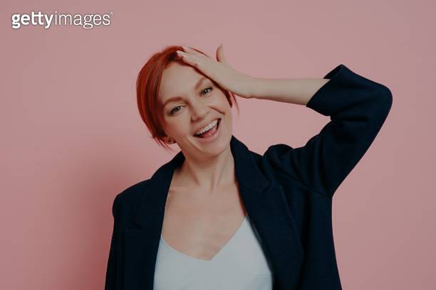 Pleased carefree ginger woman touching forehead with hand and smiling ...
