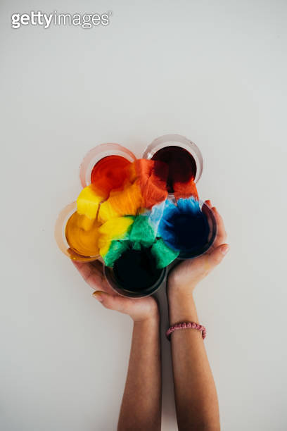 child’s hands holding rainbow food color experiment with paper and ...