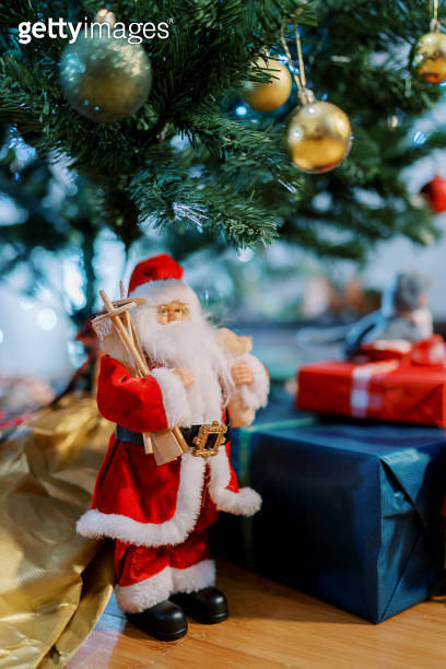 Santa Claus figurine stands near colorful gifts under a decorated ...