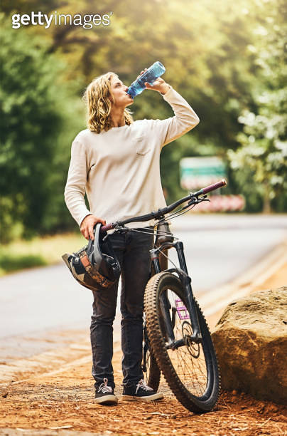 Health, cycling and man drinking water on a break in nature to hydrate ...