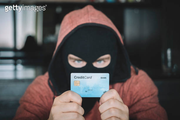 A thief in a black mask holds a stolen bank card in his hands. Skilled ...