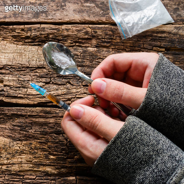 drug addict holding spoon with drug in hand and a syringe on a wooden ...