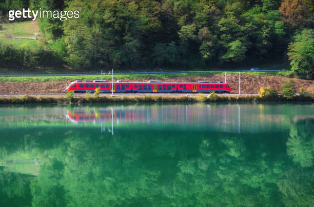 Beautiful red modern high speed train and river in alpine mountains at ...