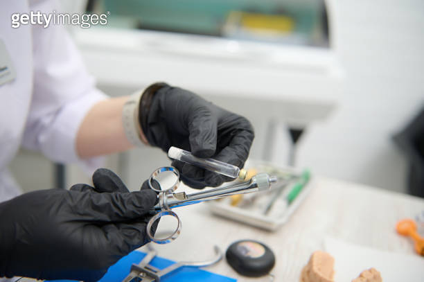 Close-up dentist hands placing a cartridge with dental anesthesia in ...