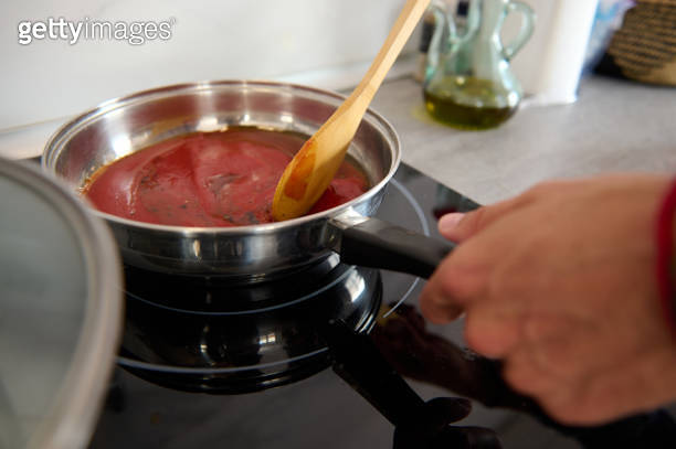 Close-up chef hand using a wooden spoon, seasoning and mixing a boiling ...