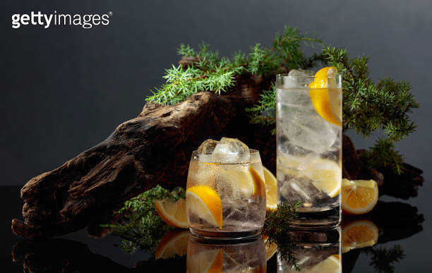 Cocktail gin-tonic with ice and lemon on a black reflective background ...