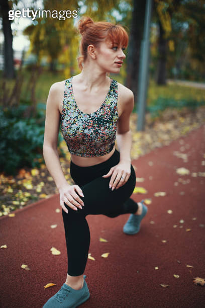 Young Caucasian redhead woman stretching before running in nature at ...