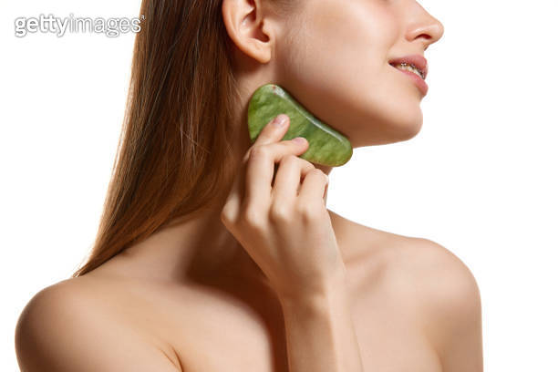 Portrait of young woman doing neck massage with natural stone scraper ...