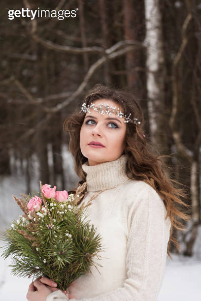 Beautiful bride in a white dress with a bouquet in a snow-covered ...
