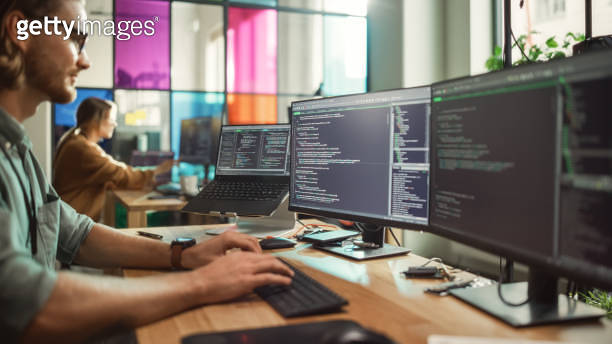 Male Programmer Coding on Desktop Computer With Two Monitors Set Up in ...