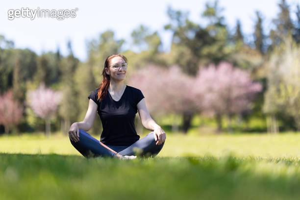 Smiling adult woman sitting in lotus position in blooming park 이미지 ...
