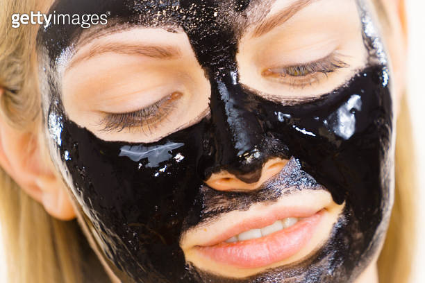 Woman applying black cleanser mask to face 이미지 (1492558436) - 게티이미지뱅크