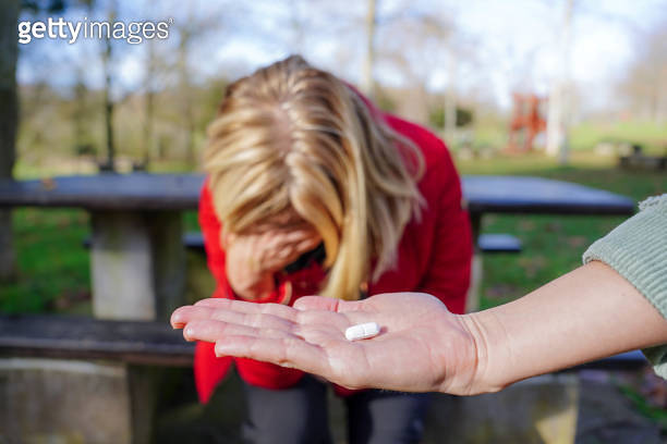 A junkie and dependent woman with her head down and a pill in the ...