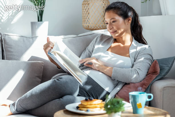 Beautiful relaxing pregnant woman reading a book while eating pancakes ...