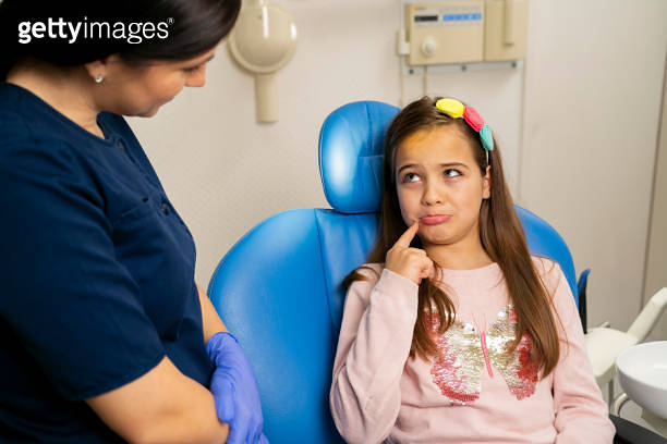 Little girl having a tooth ache pointing while talks to the dentist ...