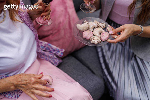 Woman offering cookies to her mother while having red wine together ...