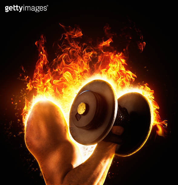 Surrounded by flames and fire, a bodybuilder's muscular arm lifts a ...