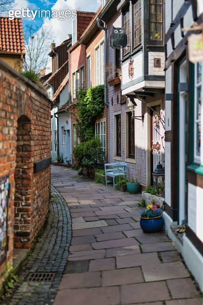 a narrow city street with a stone walkway, and several tall buildings ...