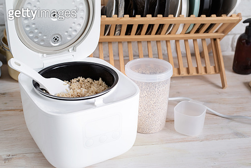 Opened electric rice cooker with cooked steaming brown rice on wooden ...