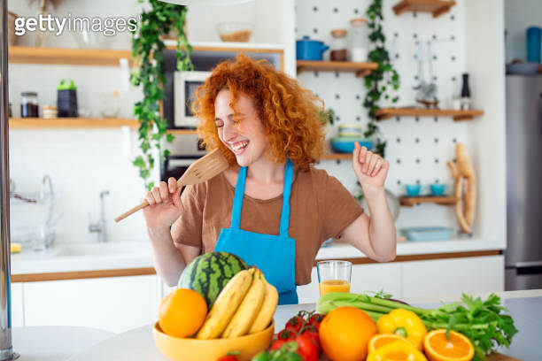 Woman joyfully sings, using a wooden spatula as a microphone. Her ...