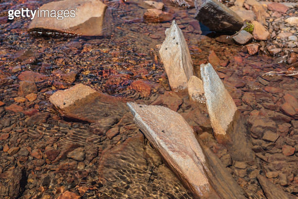 Sharp stone in clear water stream with motley stony bottom in sunlight ...