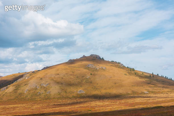 Dramatic mountain landscape with sunlit large hill with sharp rocks and ...