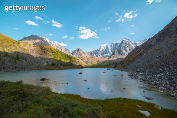 Pure azure alpine lake with view to forest hill and giant snow ...