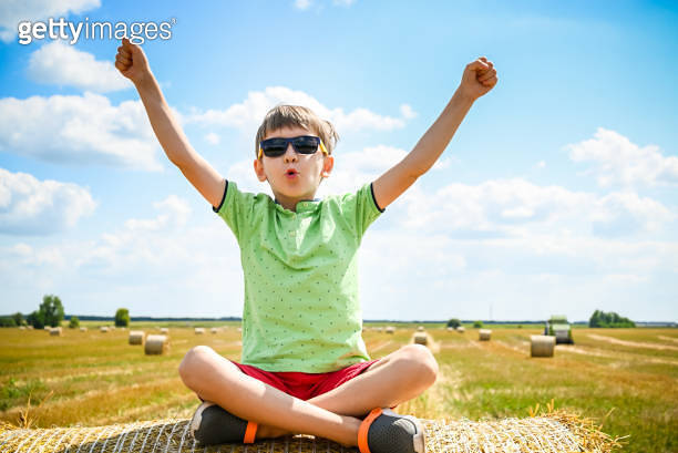 Little boy sits on a round haystack relaxed with hands up. Field 이미지 ...