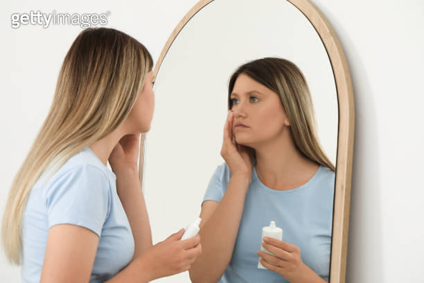 Sleep deprived young woman covering up dark circles with concealer near ...