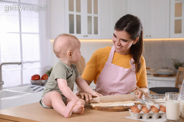 Happy young woman and her cute baby cooking together in kitchen 이미지 ...