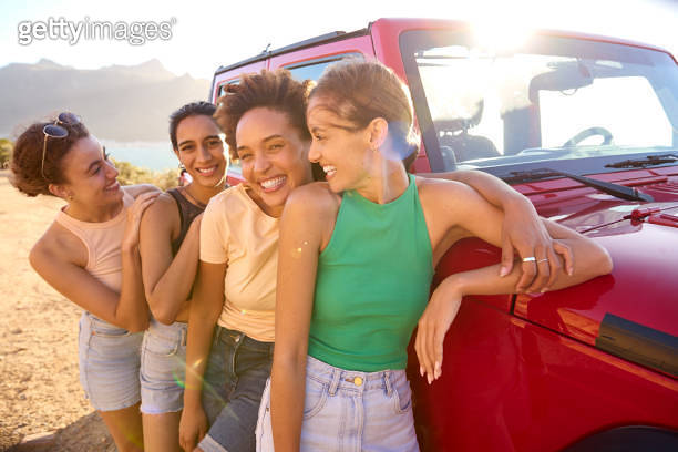 Laughing Female Friends On Vacation Having Fun Standing By Open Top Car ...